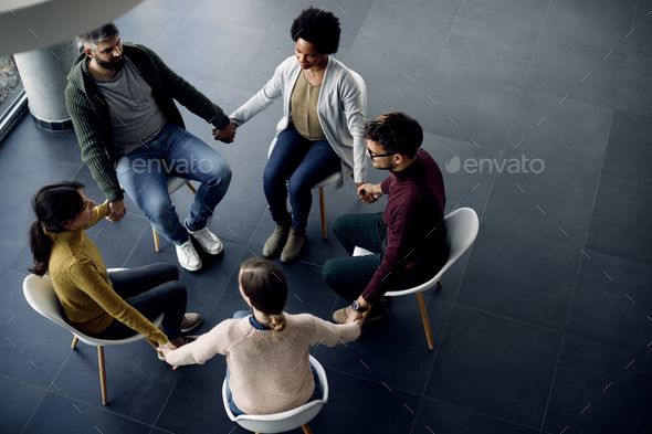 Above view of supportive people holding hands during group therapy ...