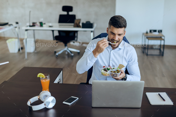 Young businessman eating healthy food while using computer on lunch ...