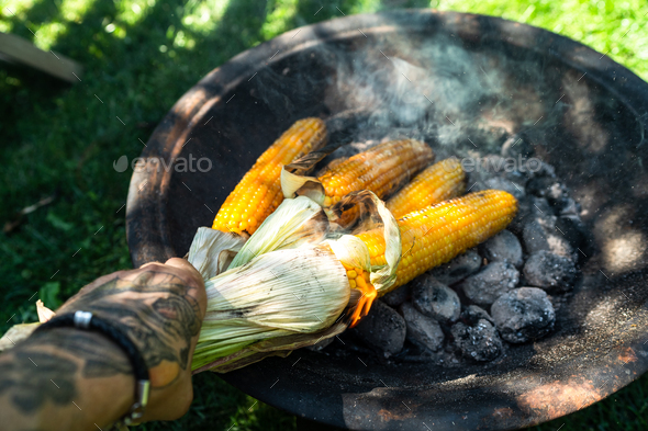 Roasting corn cobs on hot coal grill, person hand with tattoo Stock ...