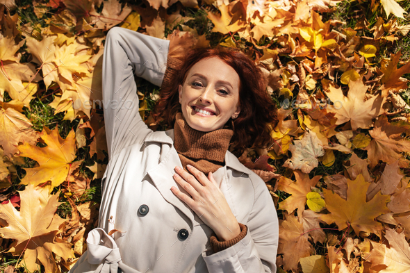 Glad happy caucasian millennial red-haired female in raincoat lies on ...