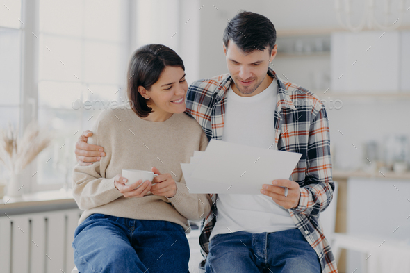 Caring man embraces his wife, look through documents with happy ...