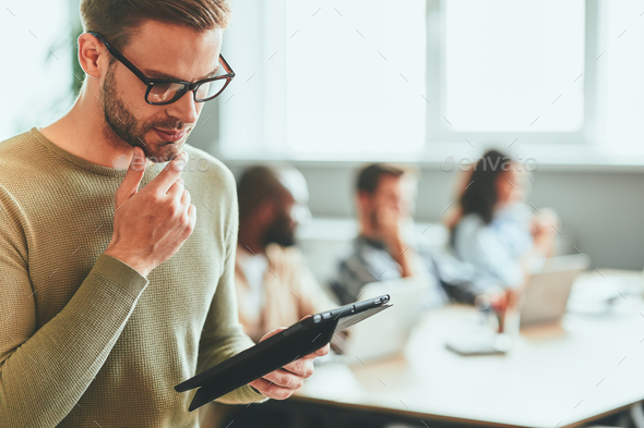 Puzzled young office worker using tablet at workplace Stock Photo by ...