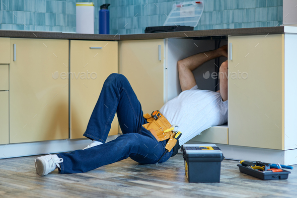 Efficient work. Professional plumber wearing tool belt fixing sink pipe ...