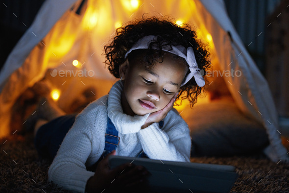 Shot of an adorable little girl using a digital tablet during bedtime ...