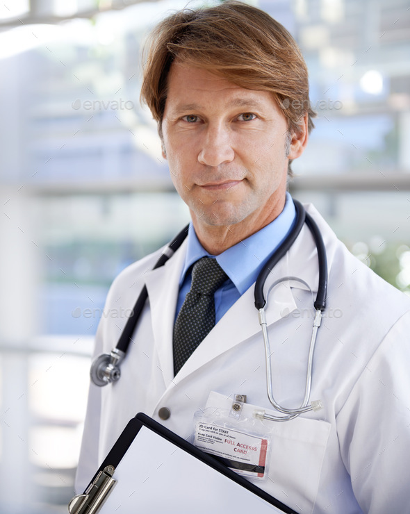 A handsome doctor standing in a hospital corridor holding a clipboard ...