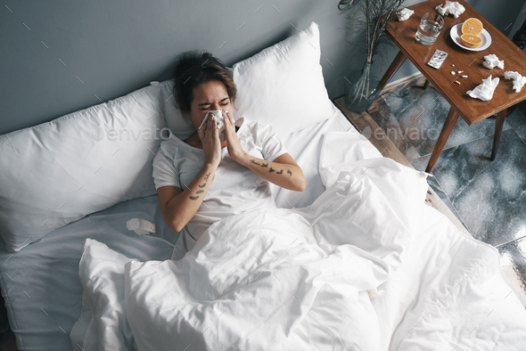 A sick girl blows her nose with tissues in bed Stock Photo by yosss1