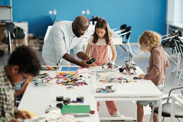 Young teacher bending over table with constructor details and ...