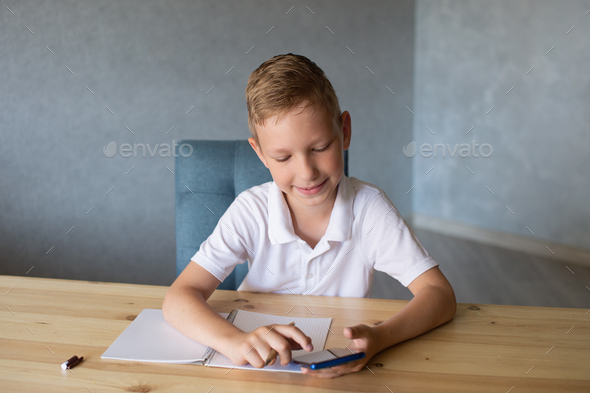 Cute boy writes in an open notebook and looks at the phone. Stock Photo ...