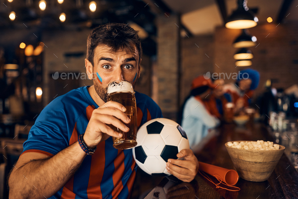 Young soccer fan holding a ball and drinking beer in pub. Stock Photo ...