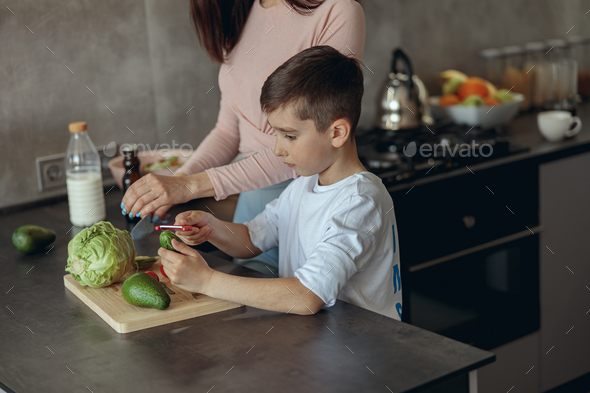 Cute little Caucasian boy helping mother to cut and cook vegetables in ...
