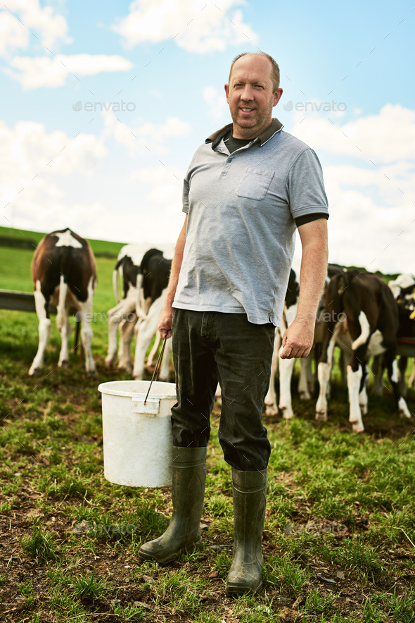 Full length portrait of a male farmer standing with a bucket of feed on ...