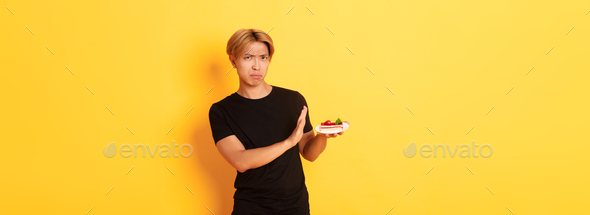 Portrait of disgusted and upset young asian guy refuse eating cake ...