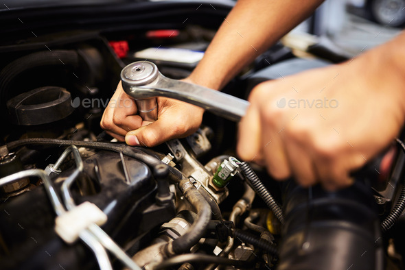 Shot of an unrecognizable male mechanic working on the engine of a car ...