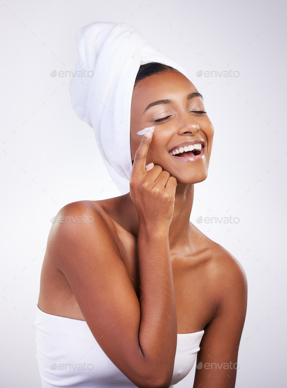Studio shot of an attractive young woman applying lotion to her face ...