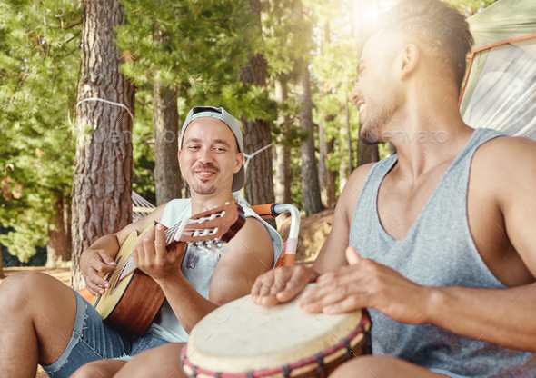 Shot of two young men sitting and playing musical instruments during a ...