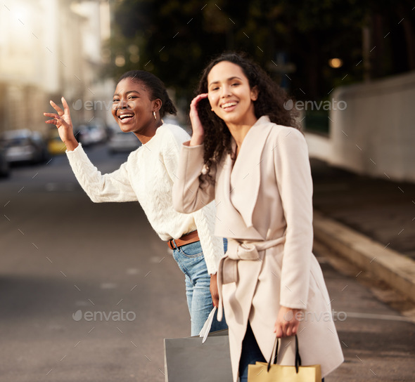 Shot of two young women calling a cab after shopping against an urban ...