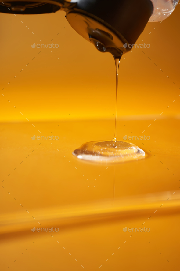 A drop of body gel or shampoo pouring from above on a yellow saturated ...