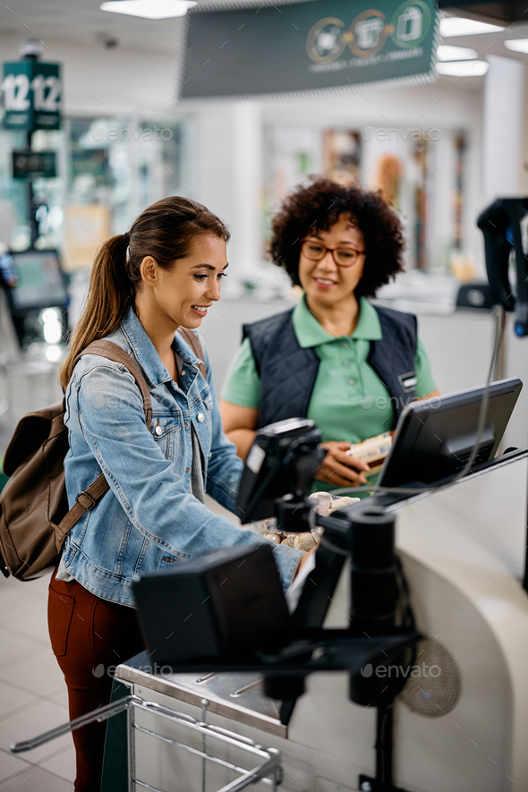 Smiling supermarket customer using self-service till with help of a ...