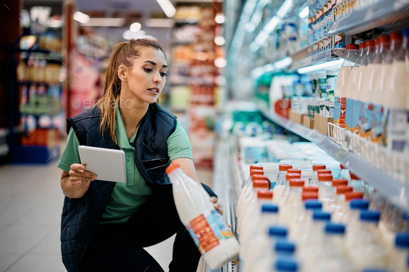 Female supermarket employee arranging products in dairy section. Stock ...