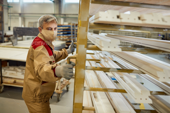 Manual worker with face mask moving rack with processed wood at ...