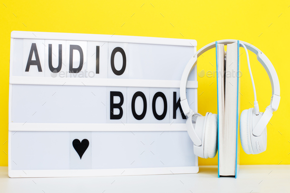 Audio book concept with modern white headphones and hardcover book on a ...