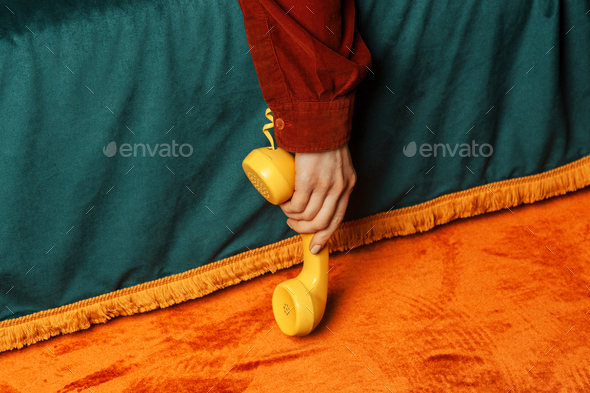 Female hand hold yellow handset of dial phone near sofa and cloth on ...