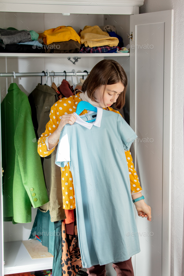 Stylish teenager girl is dressing up a clothes in wardrobe at home ...