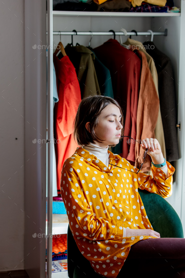 Stylish teenager girl sit in armchair next to wardrobe at home Stock ...