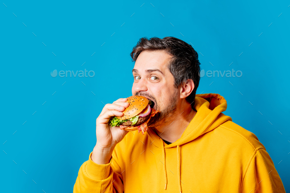 white guy in yellow hoodie eating hamburger on blue background Stock ...