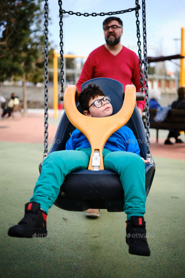 Disabled boy swinging on a special needs swing while enjoying with his ...