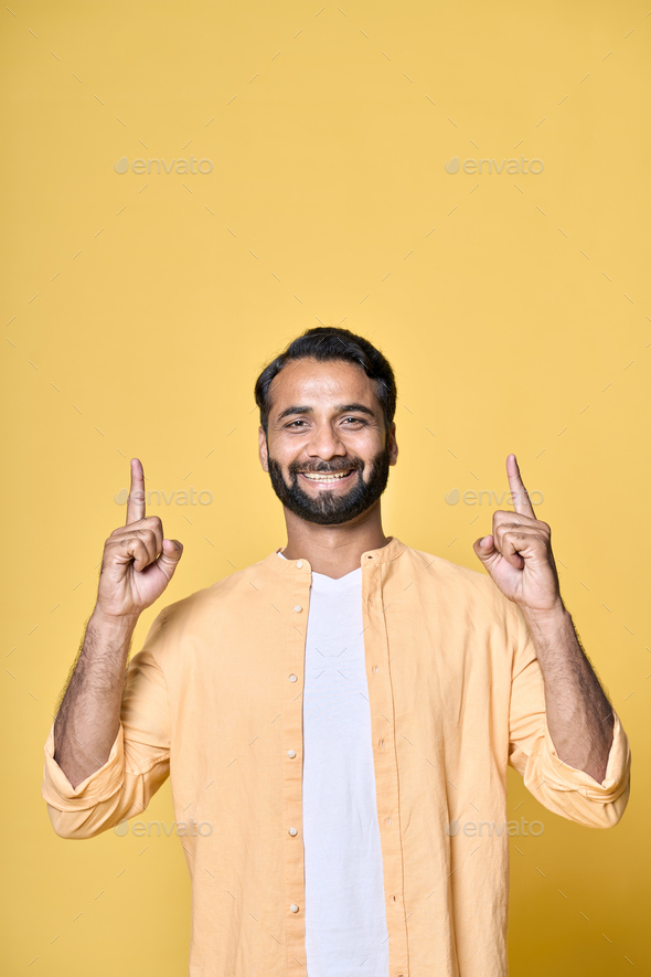 Happy indian man pointing fingers up advertising isolated on yellow ...