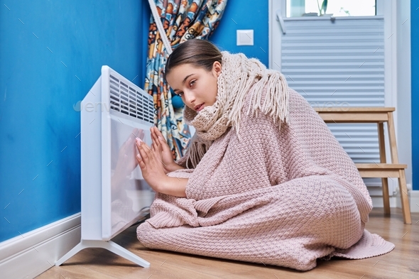 Young female sitting near an electric heater at home Stock Photo by ...