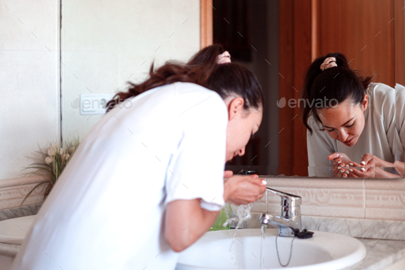 Rear view and face reflection portrait of young woman washing face in ...