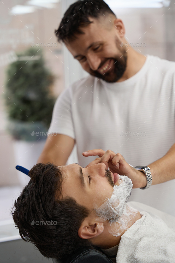 Handsome guy enjoying a professional face shave done at barber salon ...