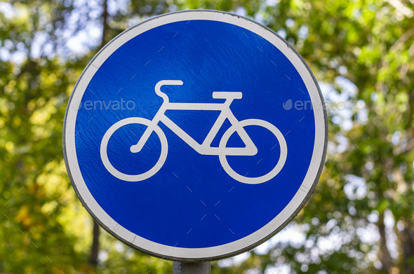 Bicycle sign on green sunny foliage backdrop. Blue and white bicycle ...