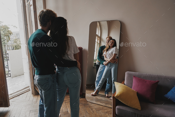 Beautiful young couple embracing and smiling while looking at their ...