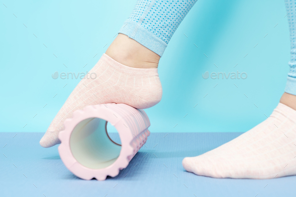 Female foot rolls a massage foam roller close-up on a blue background ...