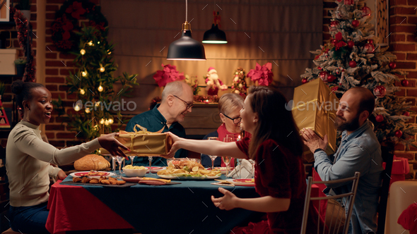 Festive family members sitting at Christmas dinner table while giving ...