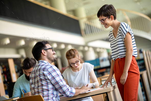 Happy university students studying with books in library. Group of ...