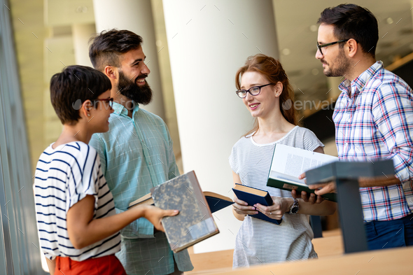 Happy university students studying with books in library. Group of ...