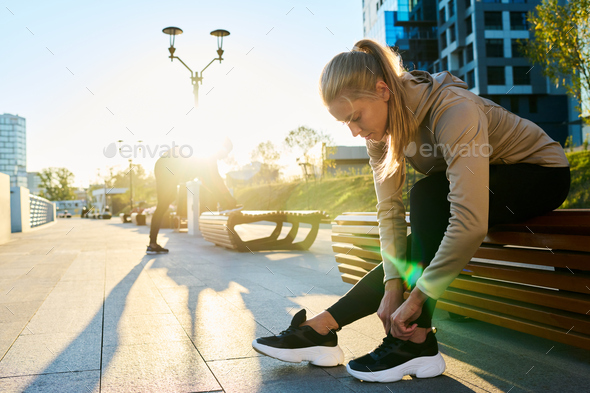 Young blond female athlete bending over leg bent in knee while sitting ...