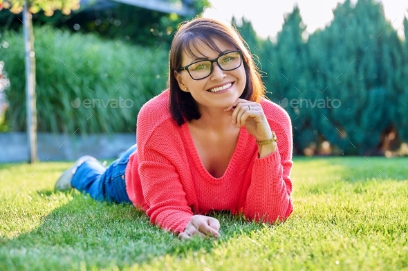 Outdoor Portrait Of Smiling Middle Aged Woman Lying On Grass Stock