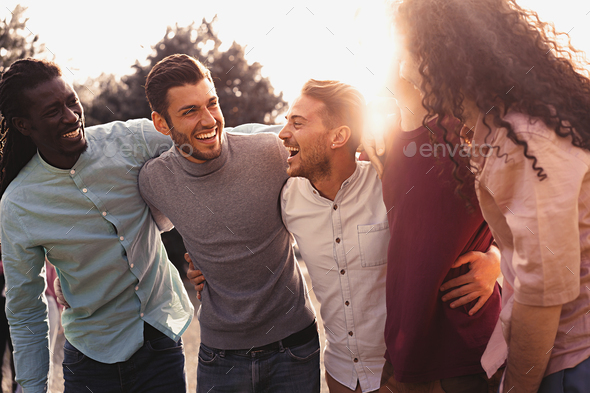 multi-ethnic group of positive friends hugging and having fun outdoors ...