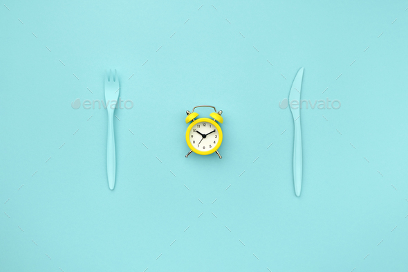 Intermittent fasting, diet, lunch time. Alarm clock and cutlery. Yellow ...