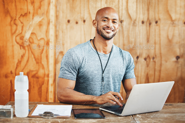 Portrait of a muscular young man using a laptop while working in a gym ...