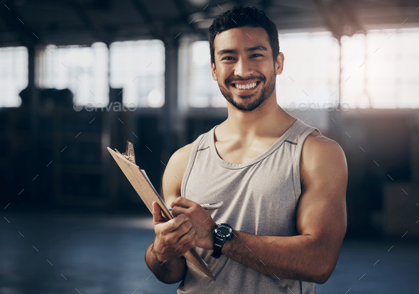 Portrait of a muscular young man writing notes on a clipboard while ...