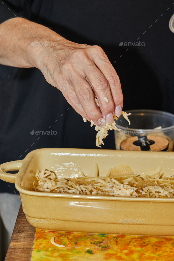 Step by step potato gratin recipe. Hands toss grated cheese onto potato ...