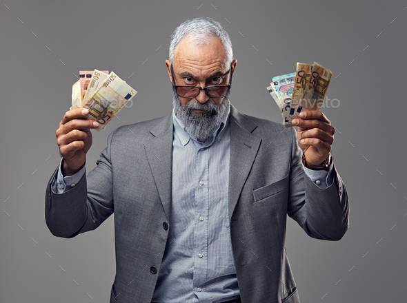 Old man with money staring at camera against grey background Stock ...