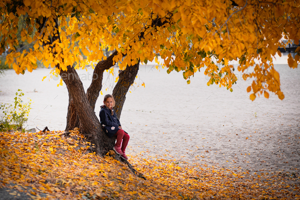 Little girl sitting under tree. Child sits alone at root of tree in ...