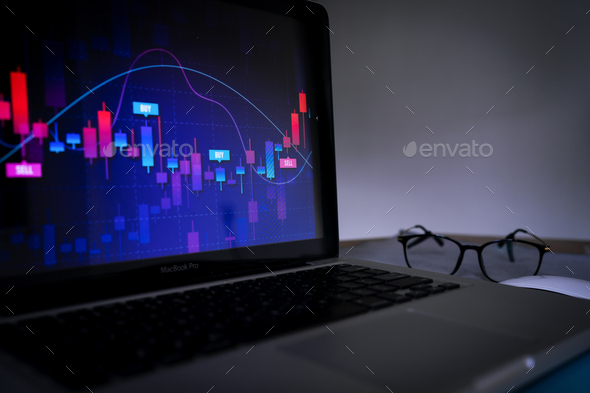 Laptop displaying a trading graph with glasses on the table Stock Photo by eelinstudio